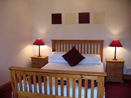 Quarto com cama de madeira, duas mesas de cabeceira e uma luminária vermelha em cada lado.