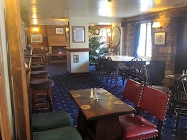 Interior de restaurante com área de bar, lareira e salão de jantar com mesas e cadeiras.