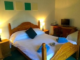 Quarto com cama de madeira, luminárias de cabeceira, televisão e uma mesinha com chaleira.