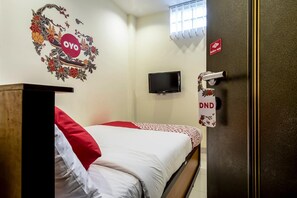 Quarto de hotel com uma cama, televisão, decoração na parede e uma porta com um aviso.