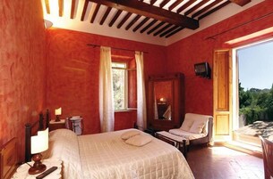 Quarto com cama, mesa de cabeceira com abajur, uma cadeira, janela com cortinas e televisão.