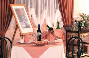 Mesa de jantar posta com taças de vinho, garrafas e um quadro emoldurado.