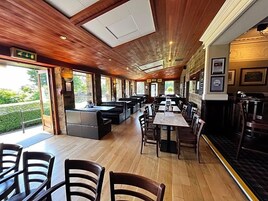 Restaurante com teto de madeira, mesas compridas e vista para o verde lá fora.