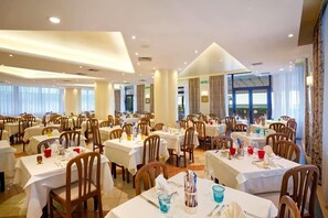 Uma sala de jantar ampla com várias mesas e cadeiras, dispostas em padrão de grade.