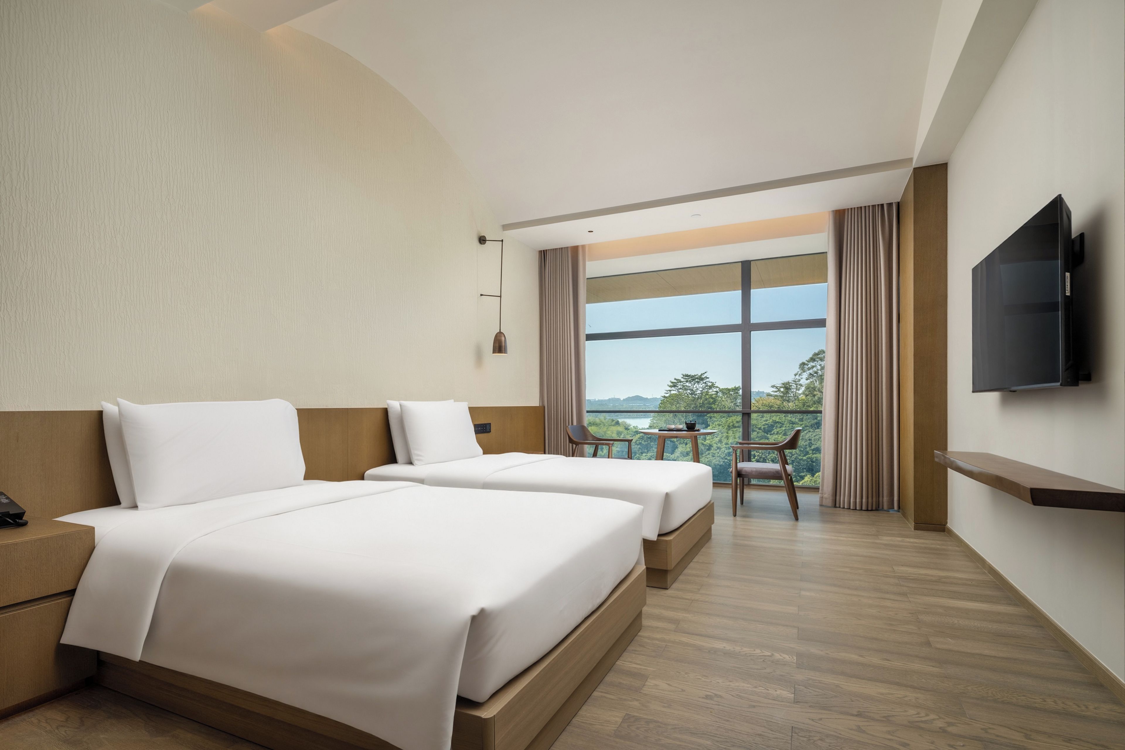 Quarto de hotel com duas camas, TV, varanda com mesa e cadeiras, e vista para o exterior.