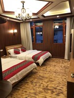 Quarto de hotel com duas camas, um candelabro, paredes de madeira e grandes janelas.