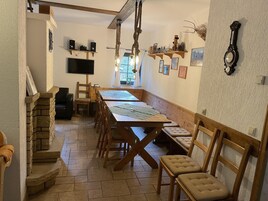 Uma sala de jantar com uma mesa de madeira comprida, cadeiras acolchoadas, uma televisão e uma escada que dá para um andar superior.