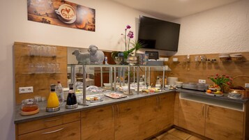 Disposição de buffet com diversos tipos de comida, uma televisão fixada na parede e uma estrutura de armário de madeira.
