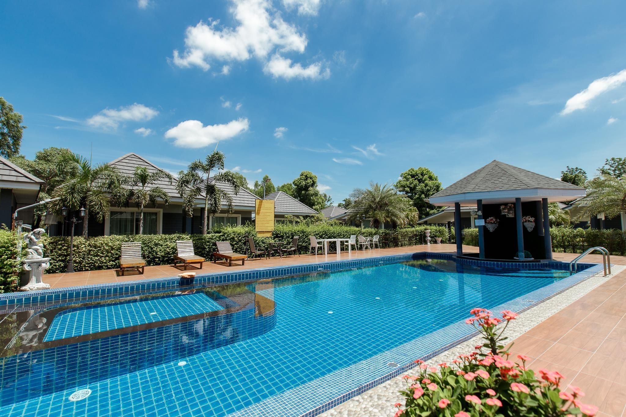 Piscina com espreguiçadeiras e um gazebo, cercada por vegetação e edifícios.
