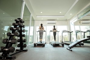 Uma academia com esteiras, um banco de musculação e halteres.