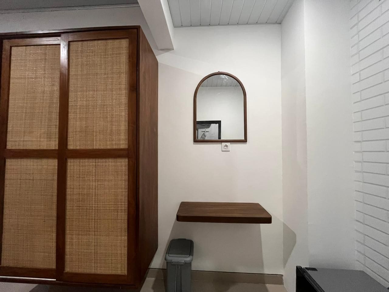Casa de banho com armário de madeira, espelho e um pequeno contentor de lixo.