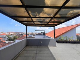 Terraço no telhado com teto de vidro, vista panorâmica da cidade e fileira de plantas.