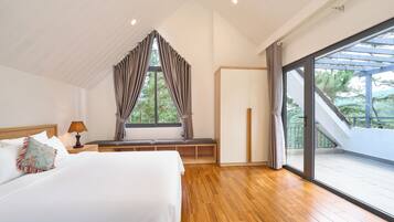 Quarto com uma cama grande, um banco, uma janela com cortinas e vista para árvores.