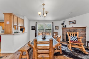 Uma sala de jantar com mesa e cadeiras de madeira, lareira e cozinha com armários de madeira.