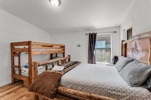 Quarto com cama beliche, uma cama de solteiro, janela com cortinas e cabeceira de madeira.