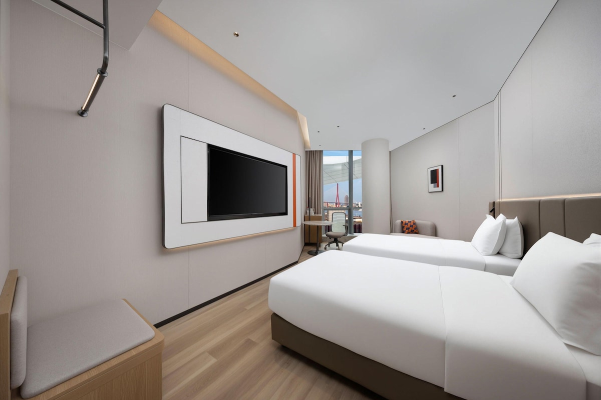 Quarto de hotel moderno com uma cama grande, escrivaninha, televisão de tela plana e vista para a cidade.