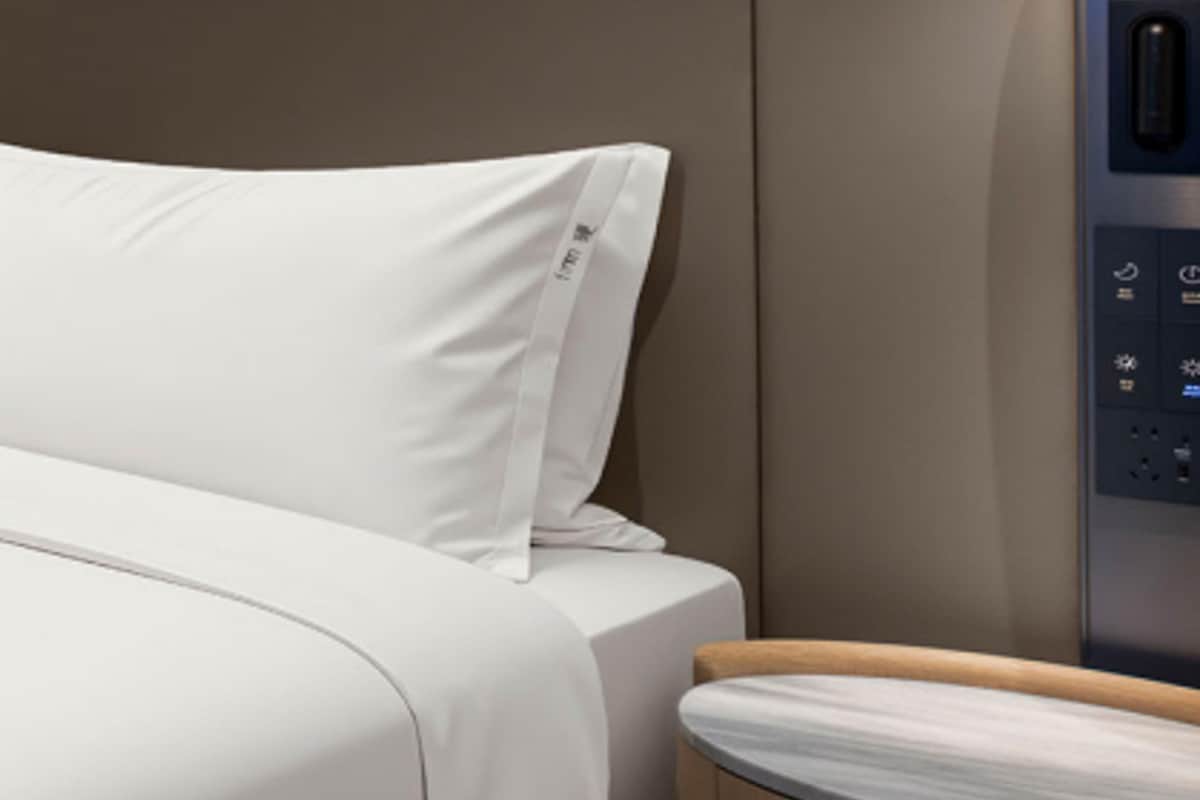 Quarto de hotel moderno com cama, uma cadeira de madeira e um painel de controle com vários botões e indicadores.