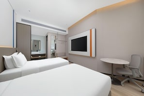 Quarto de hotel com duas camas, uma mesa, uma cadeira, televisão e banheiro com espelho e pia.