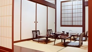 Um quarto japonês tradicional com tatames, uma mesa baixa e cadeiras, e portas deslizantes.