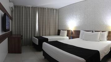 Quarto de hotel com duas camas, televisão, escrivaninha e cortina.