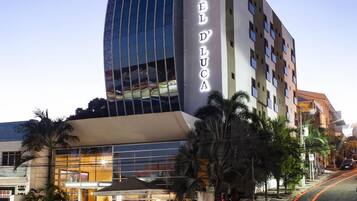 Um hotel moderno com fachada de vidro, letreiro chamativo e área de estacionamento com veículos.