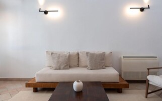 Sala de estar minimalista com sofá, mesa de centro de madeira e duas luminárias fixadas na parede.