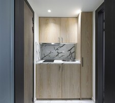 Cozinha compacta com armários de madeira, painel de fundo de mármore e pia de aço inoxidável.
