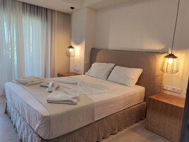 Cama bem arrumada com roupa de cama e toalhas brancas, mesa de cabeceira com abajur e janela com cortinas.