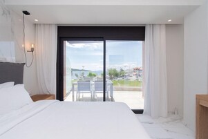 Quarto de hotel com cama grande, vista da cidade e varanda com cadeiras.