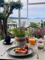 Mesa de café da manhã com vista para a água, uma árvore e uma cadeira de metal.