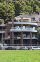 Um edifício residencial com vários andares, varandas, área de estacionamento e um gramado em primeiro plano.