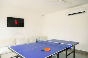 Quarto com mesa de pingue-pongue, sofá, televisão de tela plana e ar condicionado.