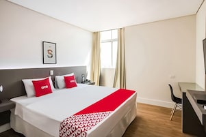 Quarto de hotel com uma cama, uma escrivaninha e uma cadeira.
