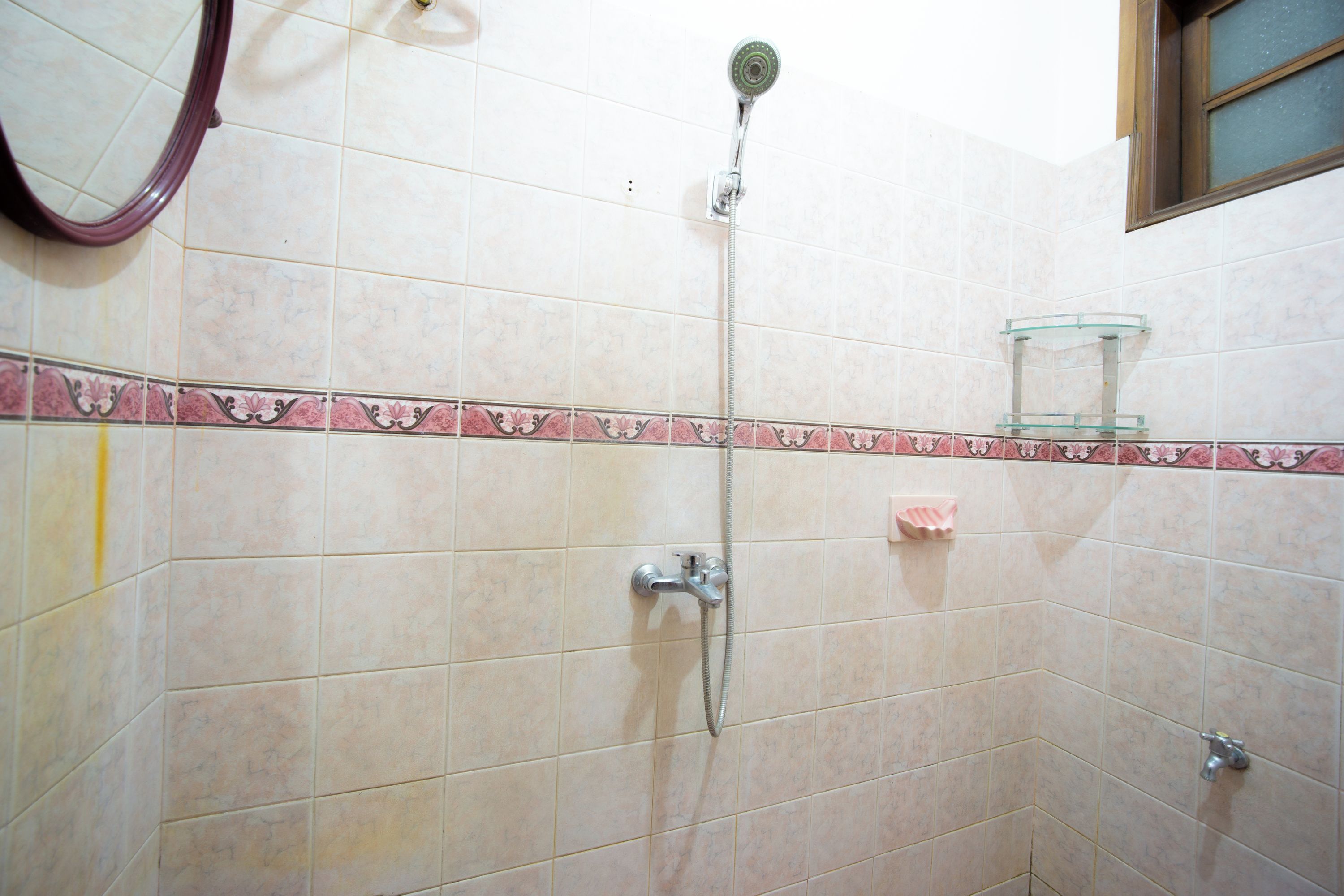 Casa de banho com chuveiro, prateleira de vidro e moldura de azulejos decorativa.