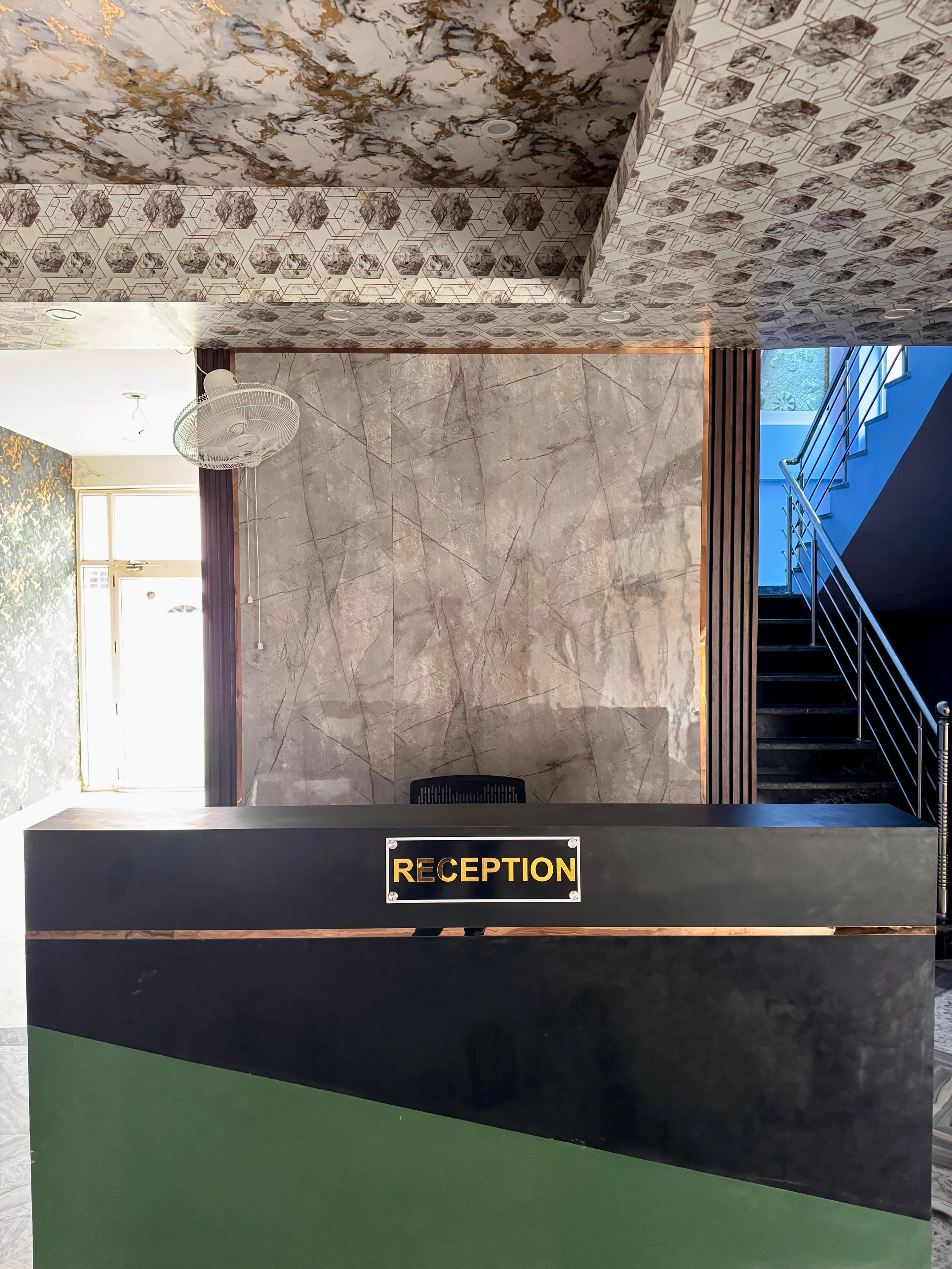 Balcão de recepção com placa 'RECEPTION', parede de mármore e escada com guarda-corpo de metal.