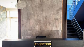 Balcão de recepção com placa 'RECEPTION', parede de mármore e escada com guarda-corpo de metal.