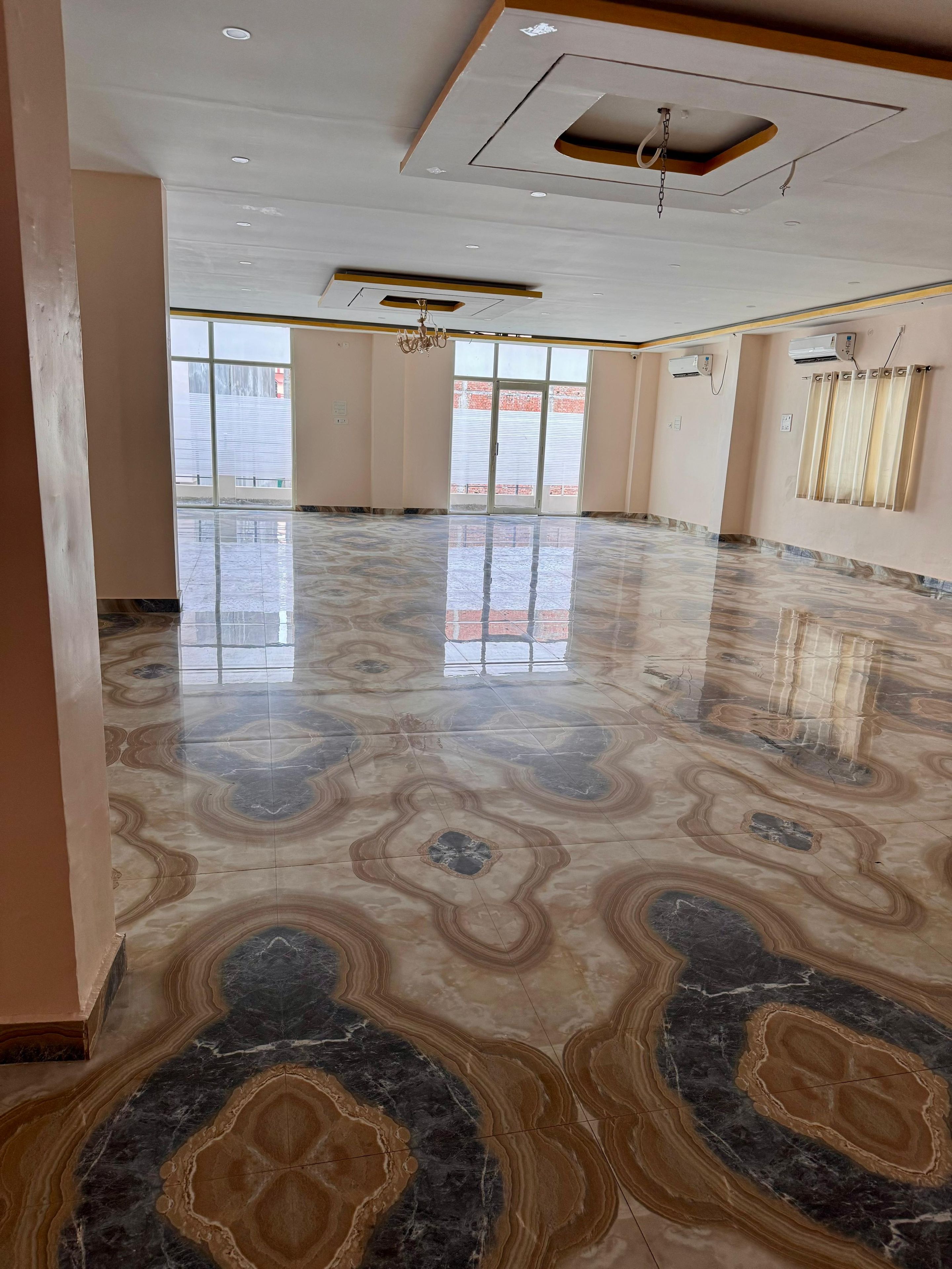 Um quarto espaçoso com piso de mármore polido, janelas amplas e unidades de ar condicionado no teto.