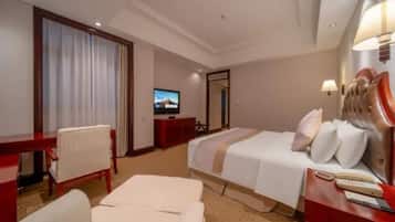 Quarto de hotel com cama, escrivaninha, cadeira, televisão e espelho.