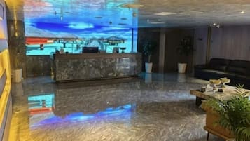 Um saguão de hotel com balcão de recepção, área de estar e uma grande tela digital exibindo uma cena subaquática.