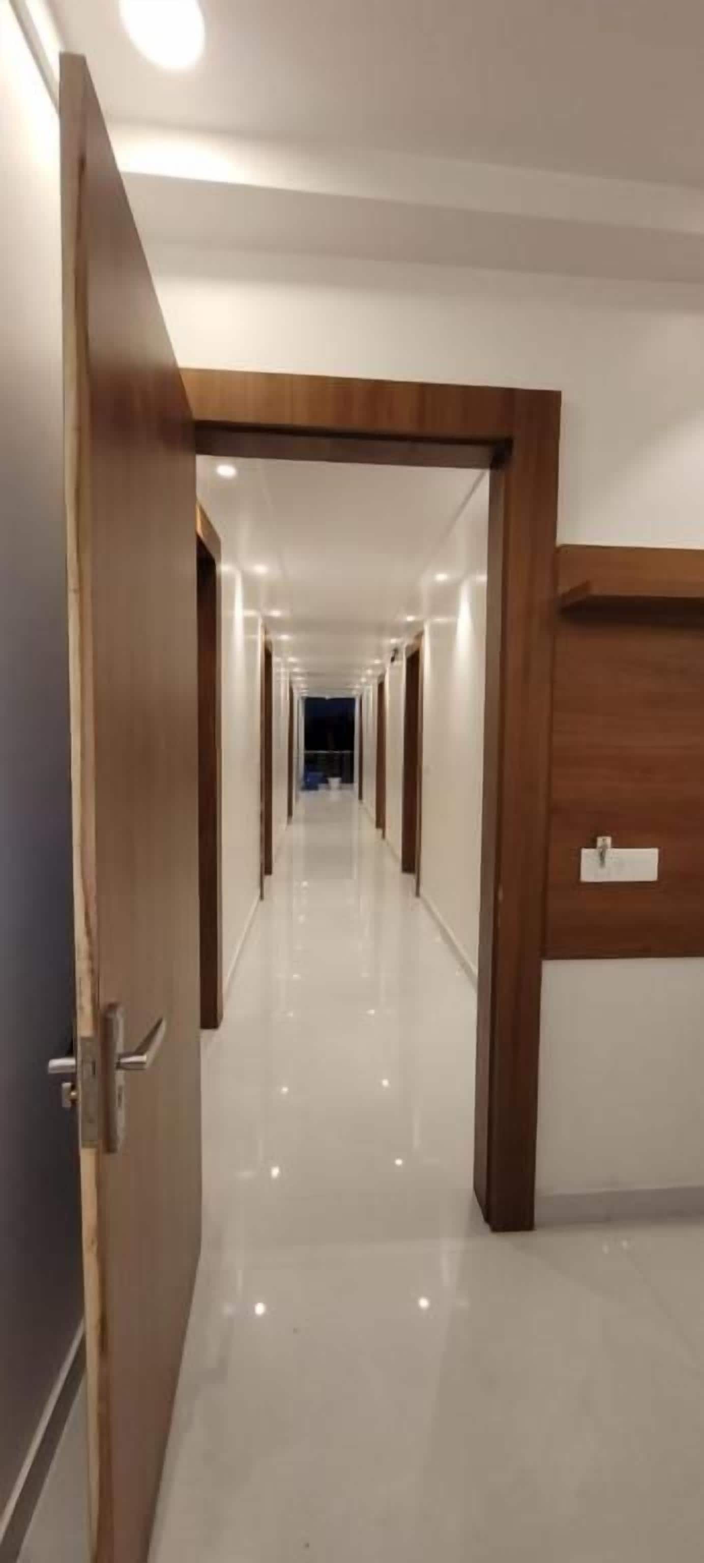 Corredor de hotel com porta de madeira à esquerda, parede de madeira à direita e chão polido.