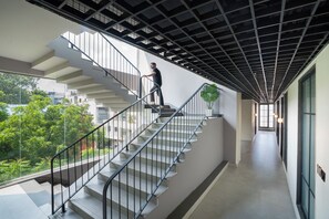 Uma escada moderna com grades de metal e balaústres de vidro, que dá para um patamar com vista para o verde lá fora.