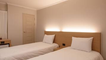 Quarto de hotel com duas camas, cabeceira de madeira, mesa de cabeceira e uma porta.