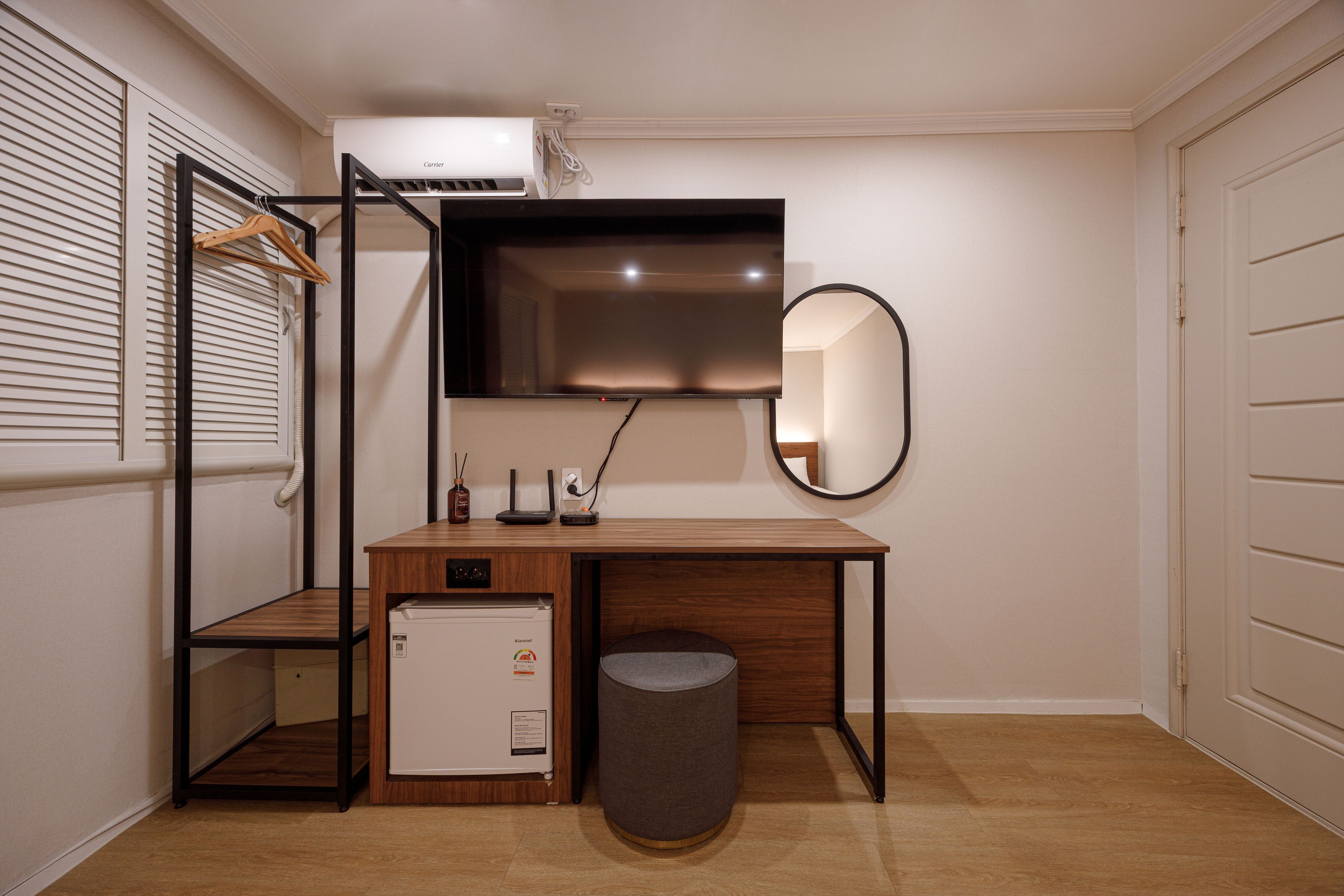Quarto compacto com beliche, pequeno frigorífico, secretária com espelho e televisão na parede.