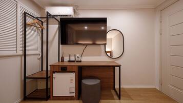 Quarto compacto com beliche, pequeno frigorífico, secretária com espelho e televisão na parede.
