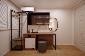 Quarto compacto com beliche, pequeno frigorífico, secretária com espelho e televisão na parede.