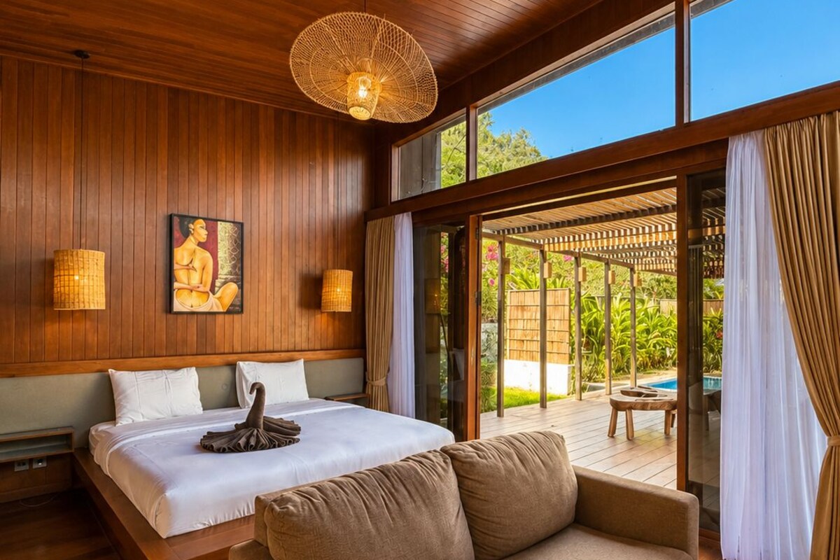 Quarto com cama grande, sofá e vista para uma piscina através de portas de vidro.