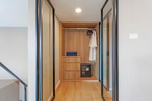 Corredor que dá para um quarto com um guarda-roupa de madeira, um banco azul e um cofre.