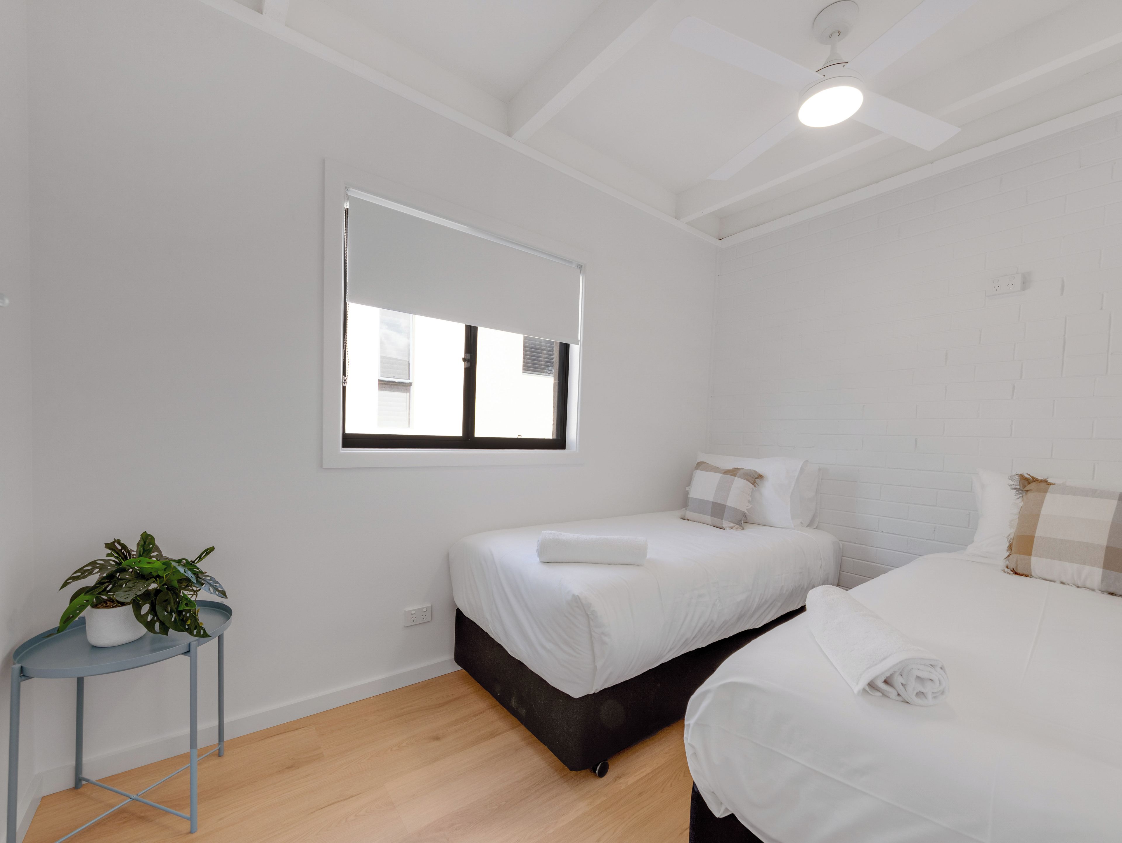 Quarto com duas camas, uma janela, um vaso de planta e um ventilador de teto.