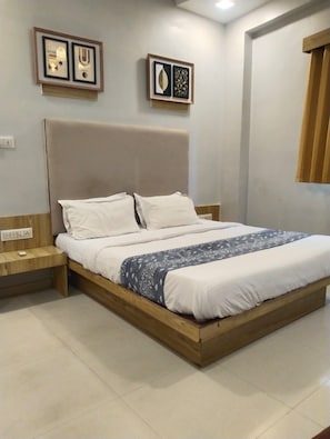 Quarto moderno com estrutura de cama de madeira, roupa de cama branca e duas obras de arte emolduradas na parede.