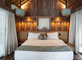 Quarto com painéis de madeira, uma cama grande, duas luminárias fixadas na parede e um objeto decorativo sobre a cama.